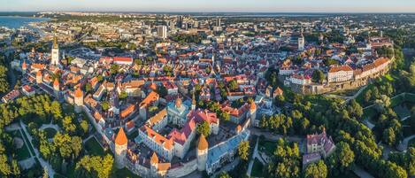 Vista aérea de uma cidade histórica com um castelo imponente, cercada por vegetação densa e uma mistura de construções tradicionais e modernas.