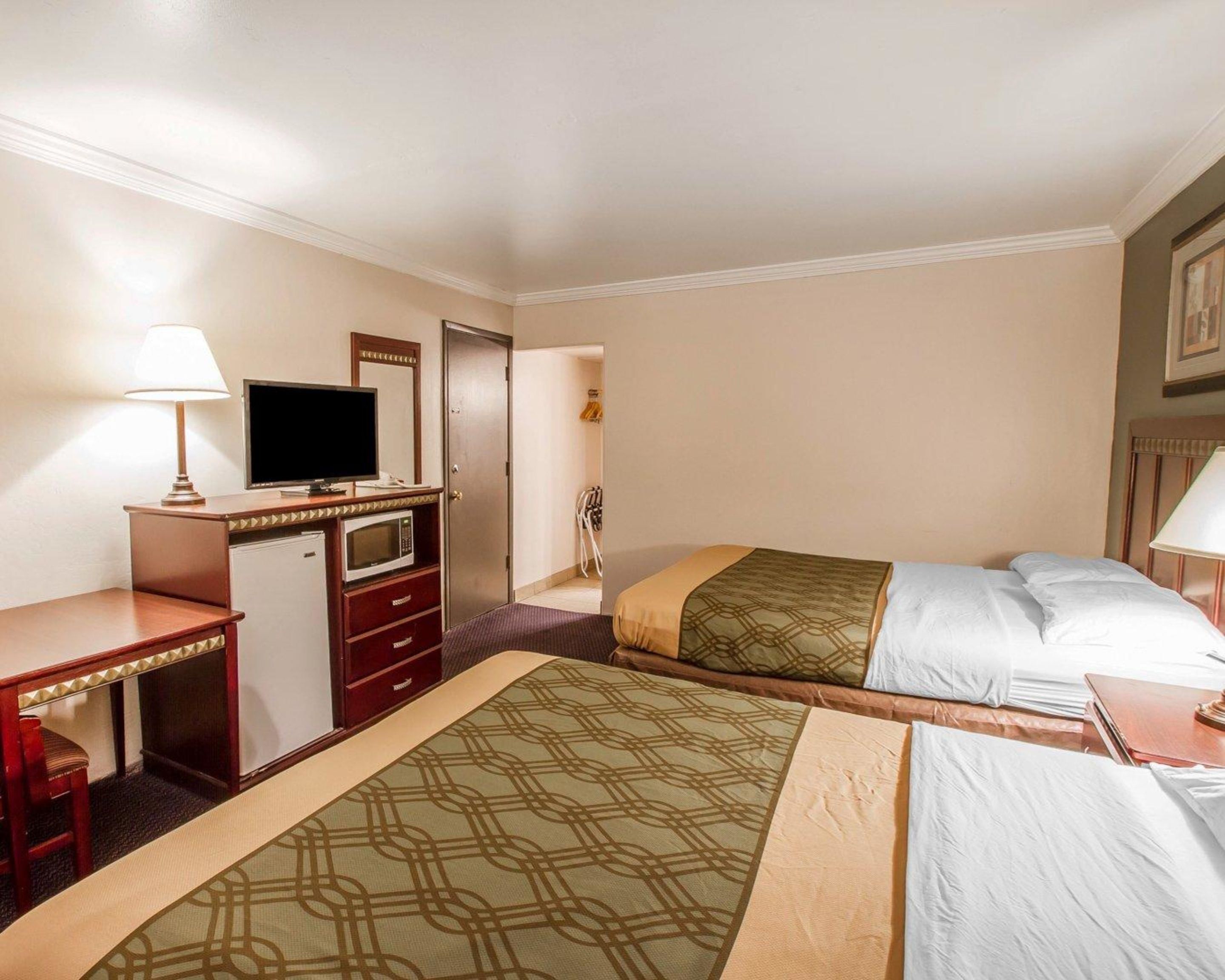 Quarto de hotel com duas camas, uma escrivaninha com televisão, micro-ondas e um guarda-roupa.