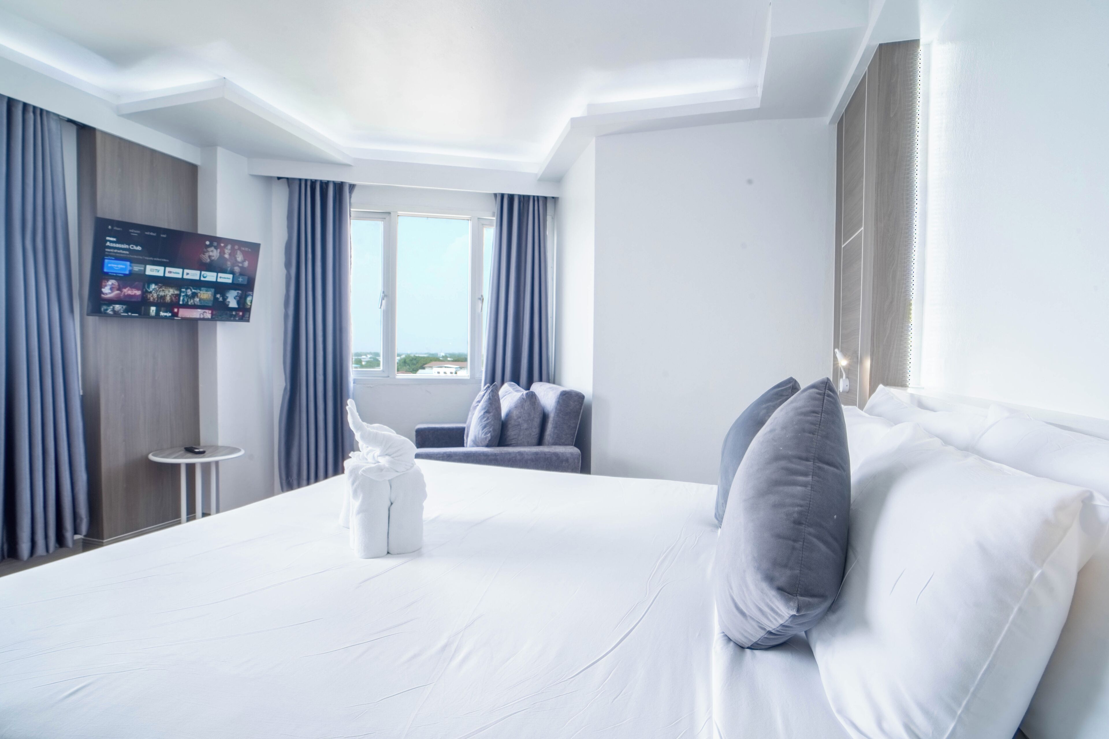 Quarto de hotel com uma cama grande, televisão de tela plana na parede, uma mesinha e vista para o exterior pela janela.