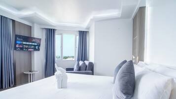 Quarto de hotel com uma cama grande, televisão de tela plana na parede, uma mesinha e vista para o exterior pela janela.