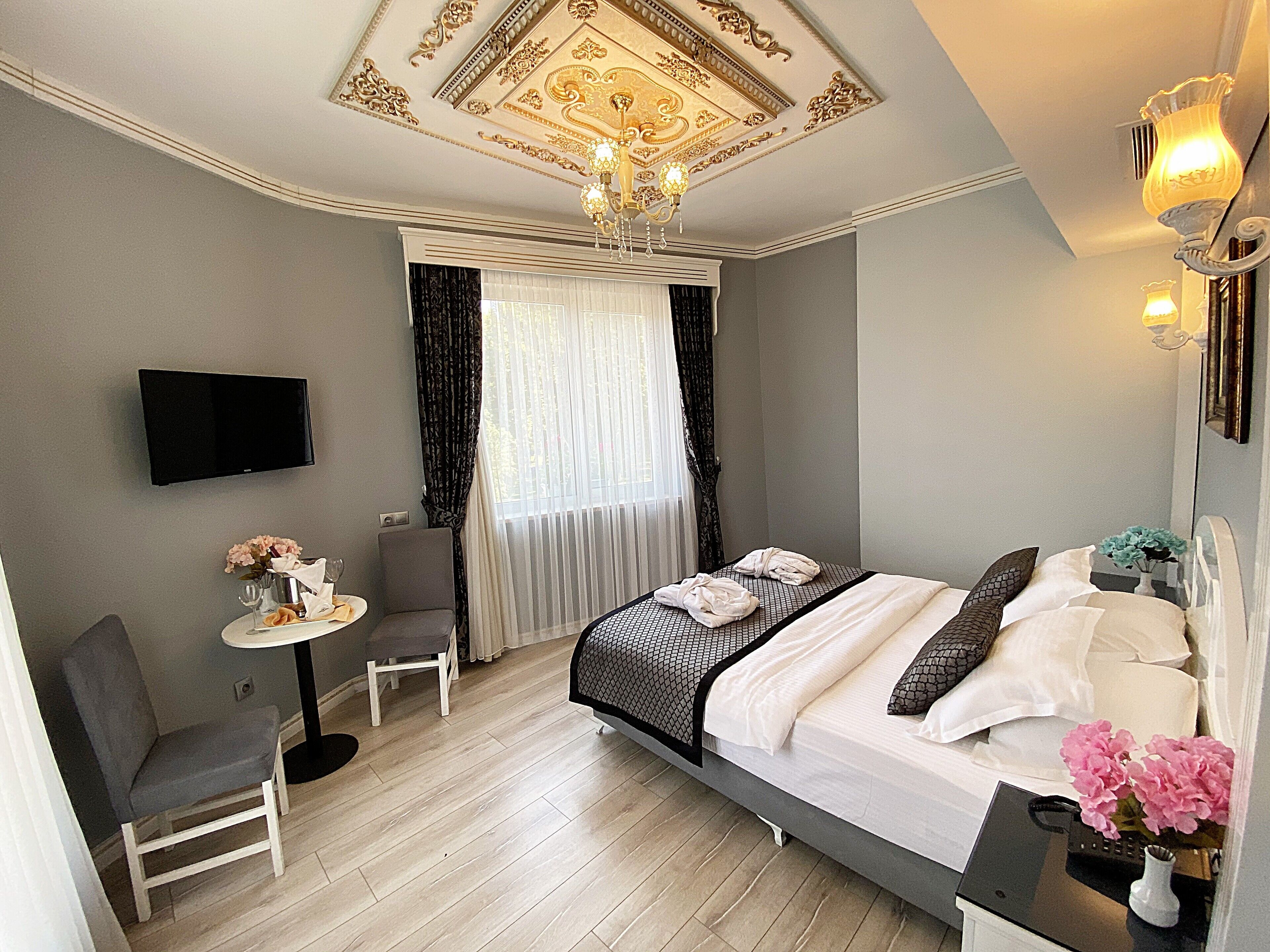 Quarto de hotel moderno com cama, escrivaninha, cadeira, televisão e um candelabro.