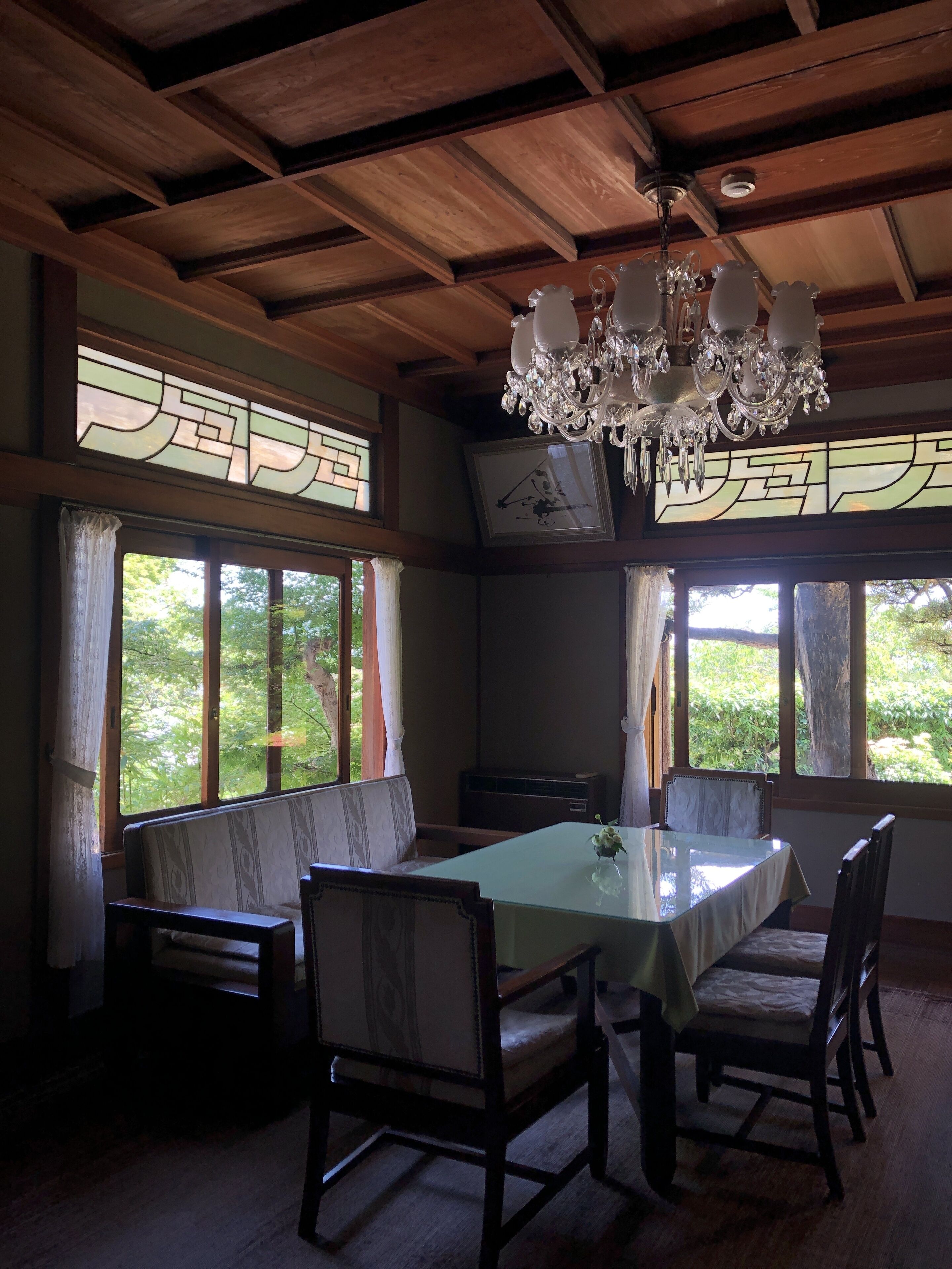 Uma sala de jantar com teto de madeira, janelas amplas com cortinas, um candelabro e uma mesa com cadeiras.