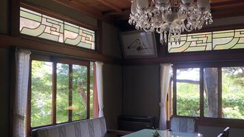Uma sala de jantar com teto de madeira, janelas amplas com cortinas, um candelabro e uma mesa com cadeiras.