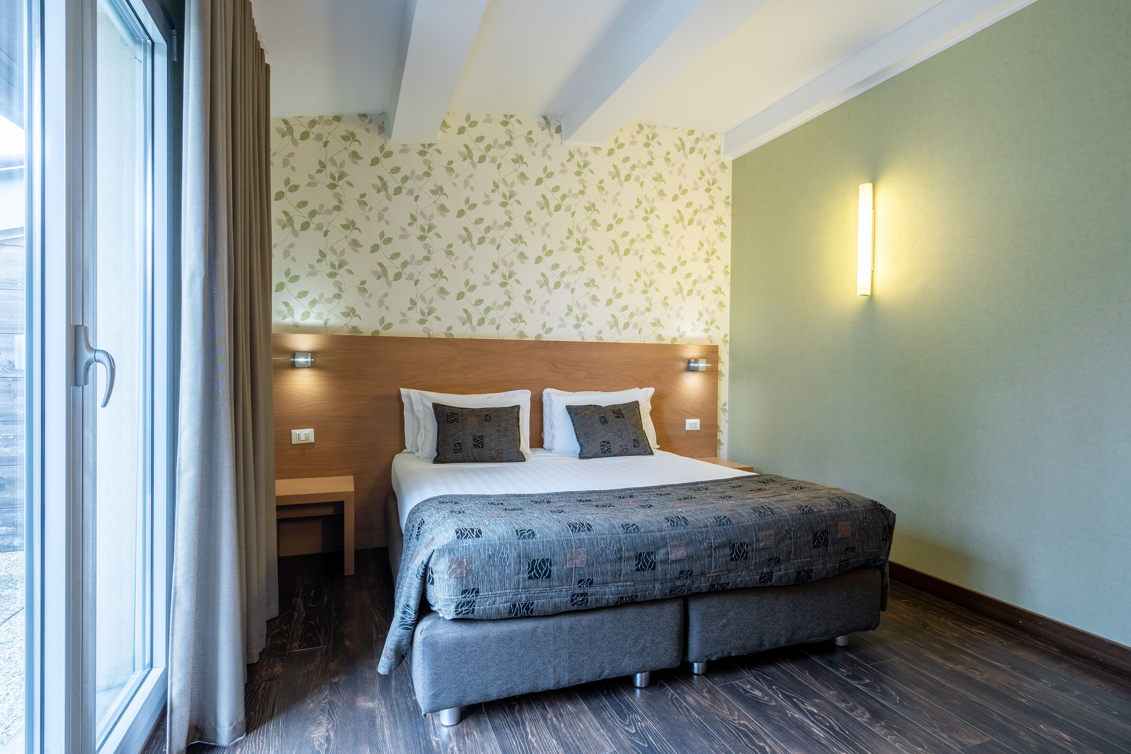 Quarto bem arrumado com cama, mesas de cabeceira e luminária fixada na parede.