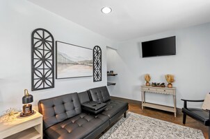 Uma sala de estar moderna com sofá de couro preto, televisão montada na parede, arte decorativa e um console com vasos.