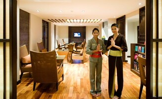 Um saguão de hotel com balcão de recepção, área de estar e uma tela de televisão.