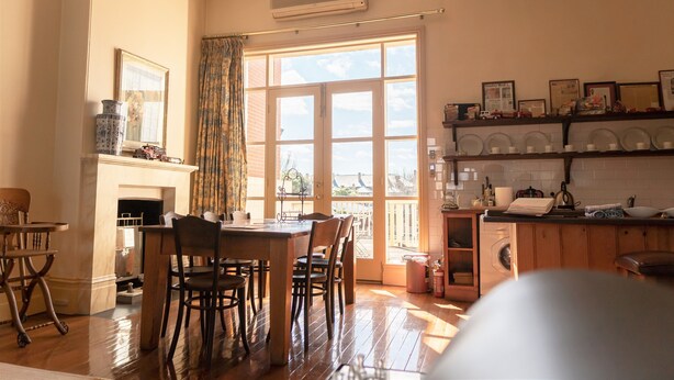Uma sala de jantar com mesa e cadeiras de madeira, lareira e uma janela grande com cortinas.