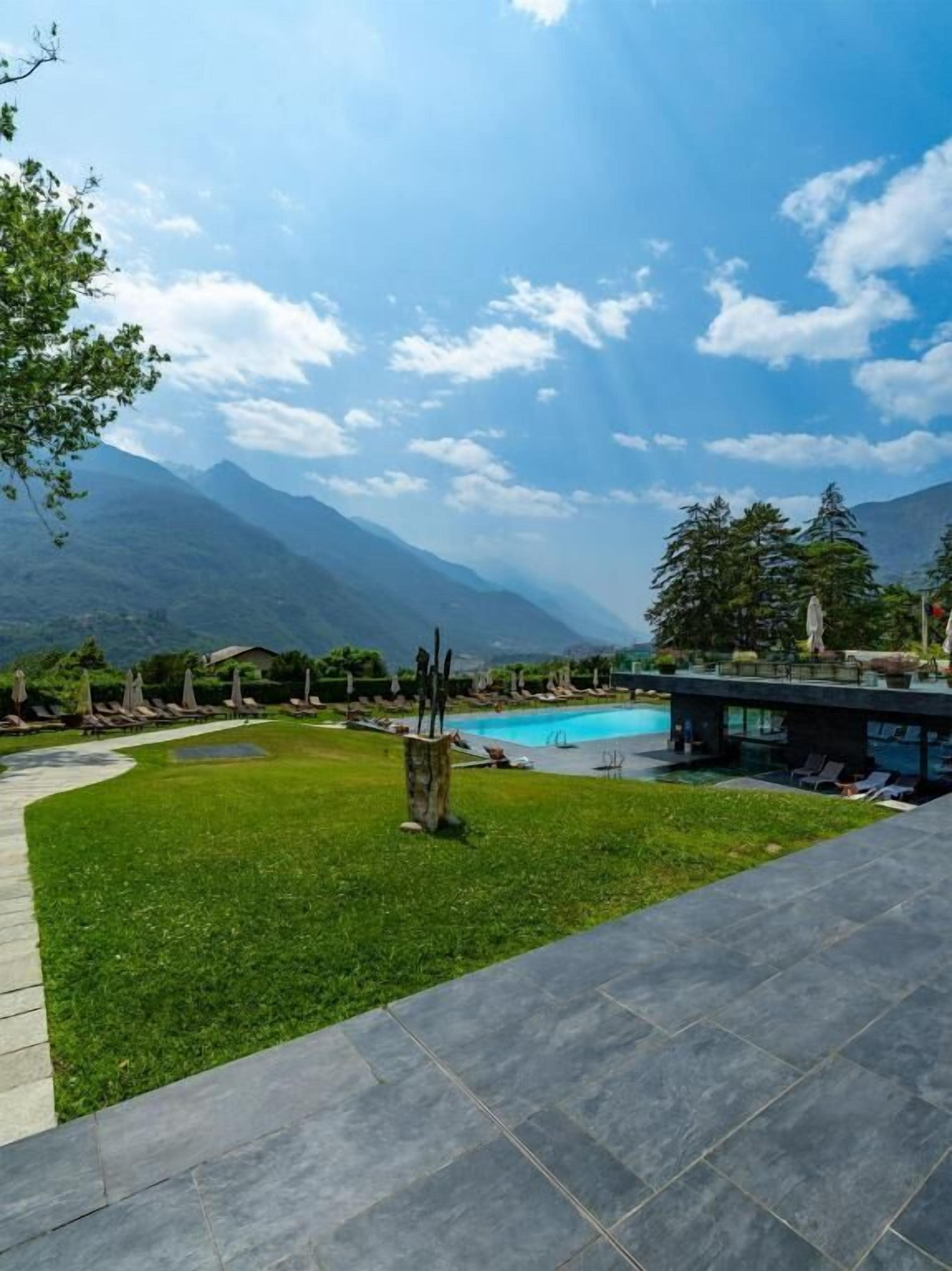 Uma área de piscina com vista para montanhas, um gramado e um edifício moderno.