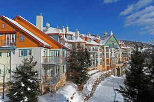 Uma fileira de edifícios coloridos de vários andares, com varandas e telhados cobertos de neve, provavelmente um hotel ou resort.