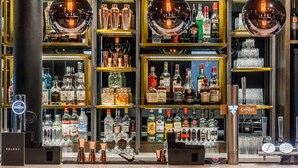 Uma área de bar com prateleiras de garrafas de bebidas, copos e uma torneira de chopp.