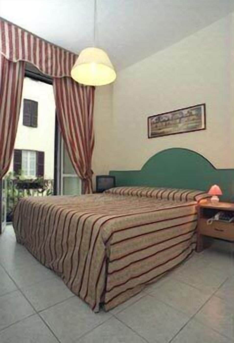 Quarto com cama, cortinas, abajur, mesa de cabeceira e um quadro na parede.