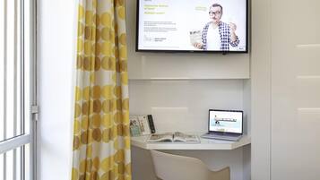 Quarto moderno com escrivaninha, um laptop e uma TV exibindo um anúncio da B&B Shop.