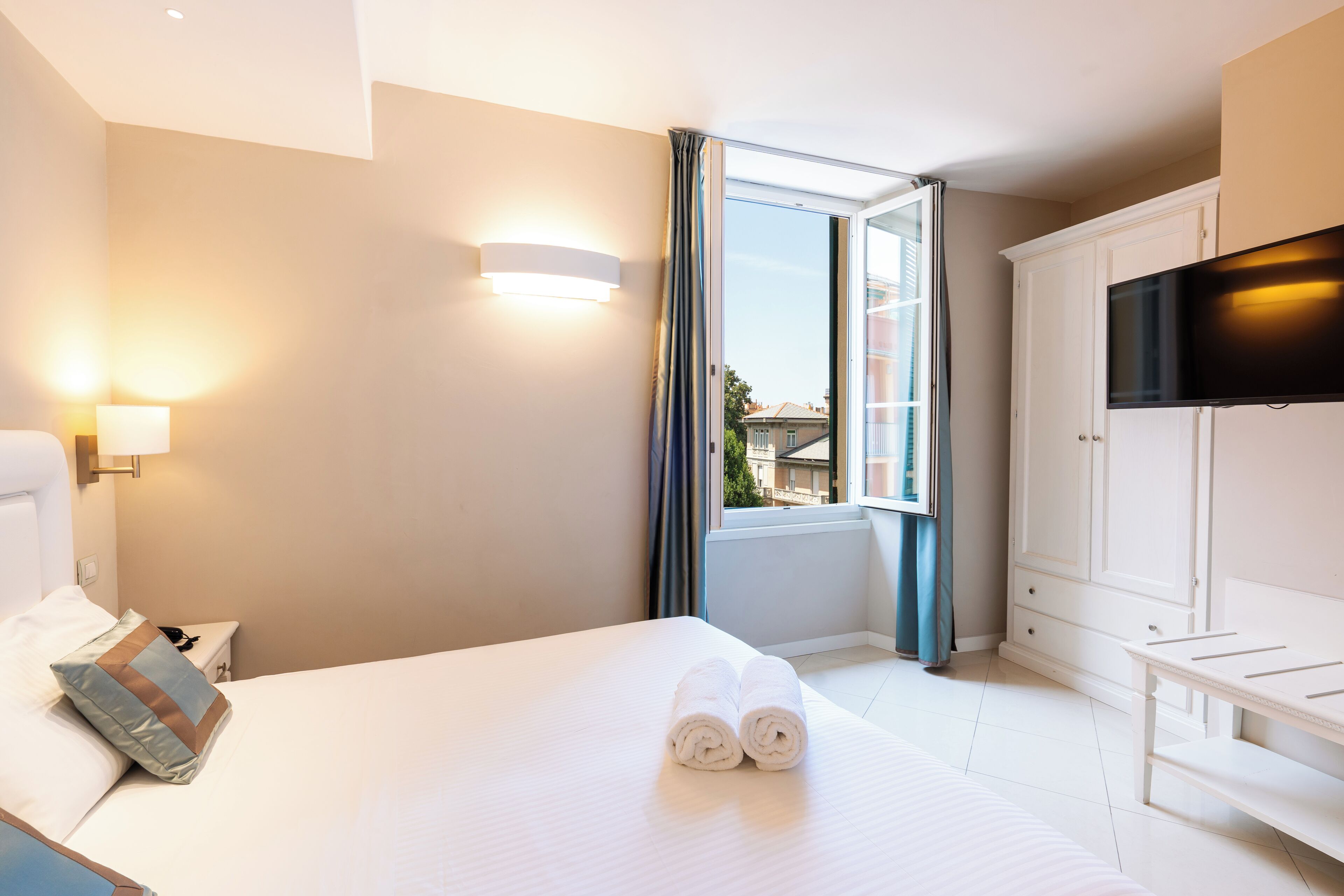 Quarto de hotel com cama, televisão, guarda-roupa e janela com cortinas.