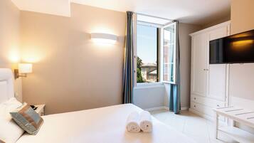Quarto de hotel com cama, televisão, guarda-roupa e janela com cortinas.
