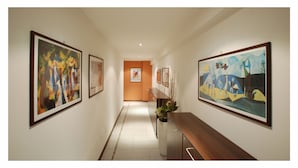Corredor com quadros abstratos emoldurados nas paredes, uma mesa de recepção e um vaso com planta.