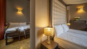 Quarto de hotel com duas camas, uma mesa de cabeceira com abajur e arandelas decorativas na parede.