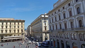 Uma praça animada com edifícios históricos, uma fonte central e áreas de estar ao ar livre.