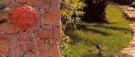Um caminho de pedra com um muro de pedra rústica de um lado e uma área gramada com plantas do outro.