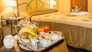 Quarto de hotel com cama bem arrumada, bandeja com itens de café da manhã e um buquê de flores na cama.