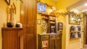 Um balcão de madeira com uma máquina de café, uma televisão e uma prateleira com copos laranja.