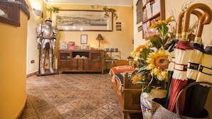 Um quarto com piso de azulejos, uma cama de madeira com colcha estampada, um armário de madeira, um mapa emoldurado na parede e uma estátua de um cavaleiro de metal.