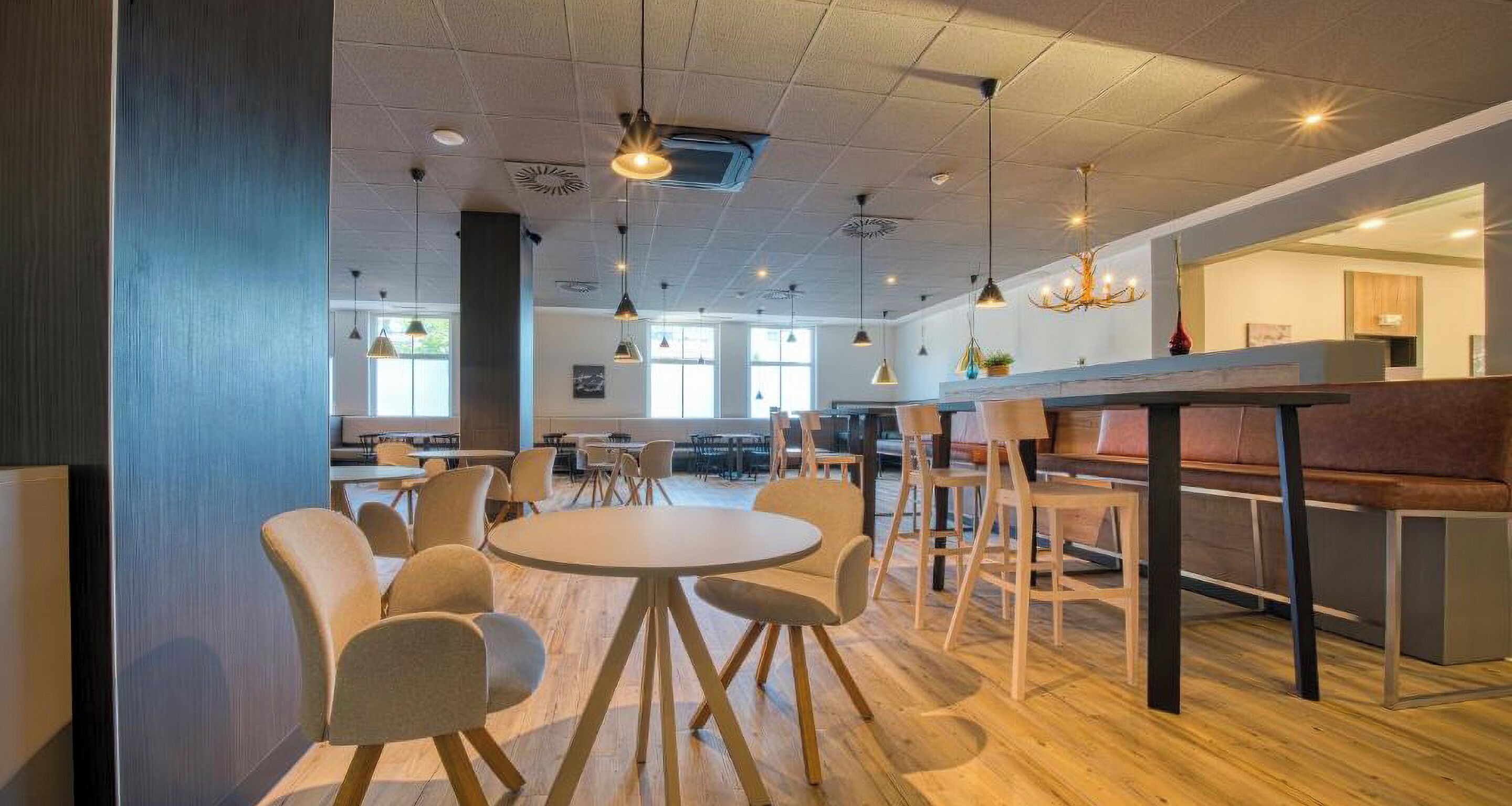 Um interior moderno com mesas e cadeiras redondas, um espaço de bar e uma cozinha ao fundo.