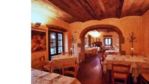Um restaurante com mesas postas para refeições, vigas de madeira no teto e um ambiente acolhedor e convidativo.