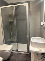 Casa de banho moderna com cabine de duche em vidro, lavatório branco e sanita.