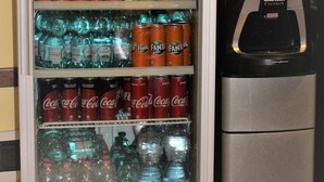 Máquina de vendas abastecida com Fanta, Coca-Cola e outras bebidas, e um extintor fixado na parede.
