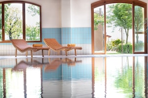 Piscina com duas espreguiçadeiras e uma toalha, rodeada por grandes janelas com vista para o verde.