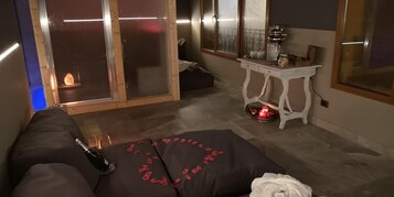 Um quarto acolhedor com um sofá, uma mesinha com uma vela e um arranjo de pétalas de rosa em formato de coração no chão.