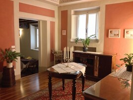 Uma sala de jantar com uma mesa de madeira, cadeiras, um candelabro e uma janela com uma planta no parapeito.