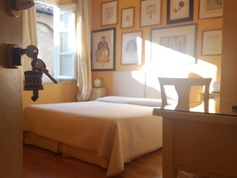 Um quarto com cama, mesa de cabeceira, cadeira e parede decorada com quadros.