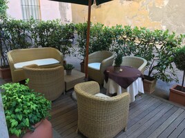 Um pátio com mobiliário de vime, incluindo dois sofás e uma mesa, rodeado por plantas em vasos.
