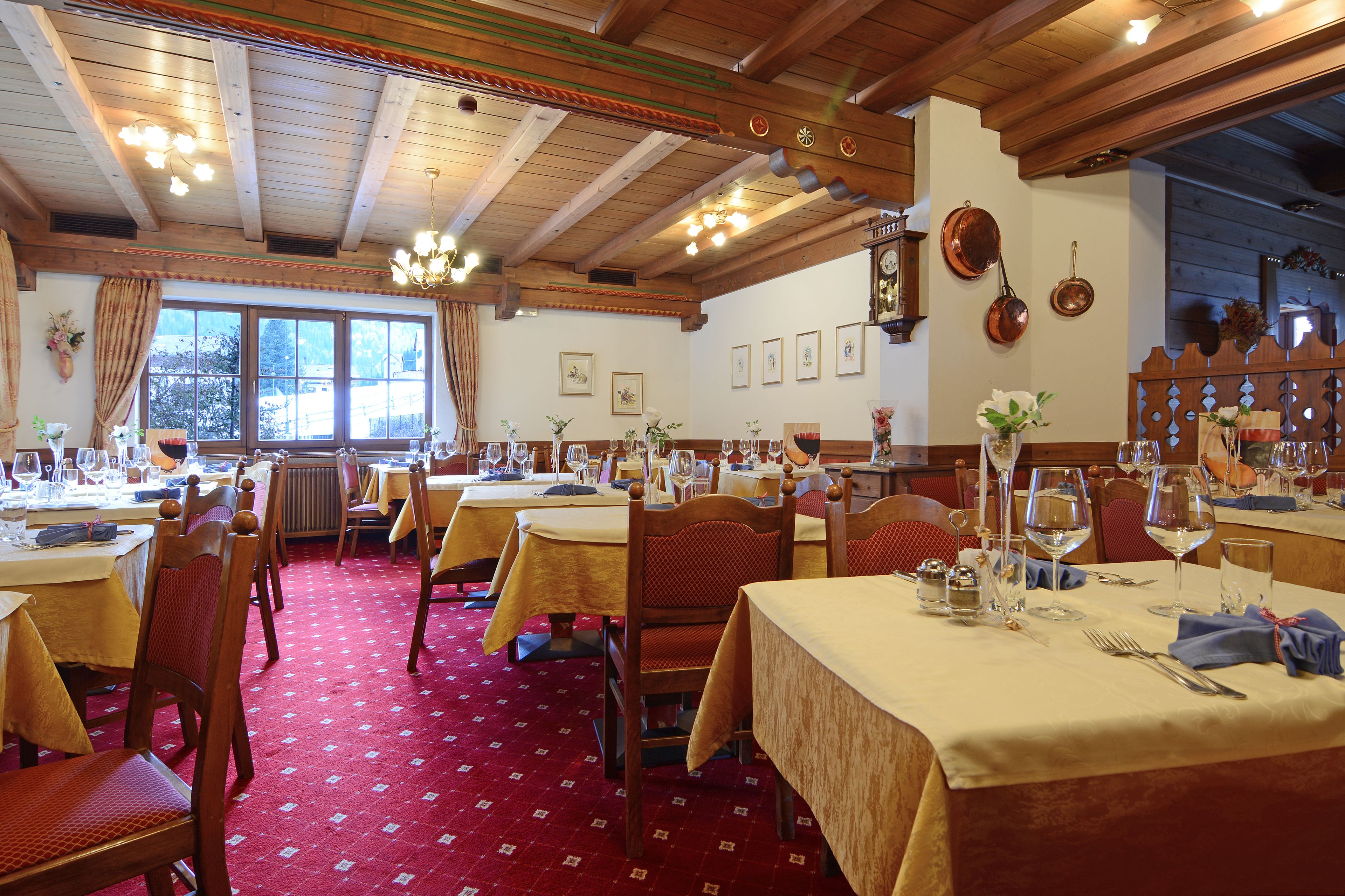 Restaurante com vigas de madeira, piso coberto por um tapete vermelho e mesas preparadas para refeições.