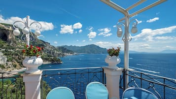 Terraço com mesa e cadeiras, oferecendo vista para a costa, montanhas e o mar.