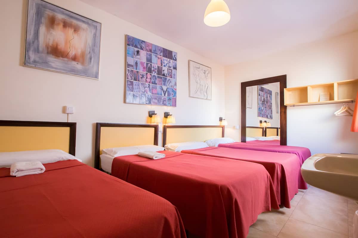 Quarto de hotel com três camas, banheira e obras de arte nas paredes.