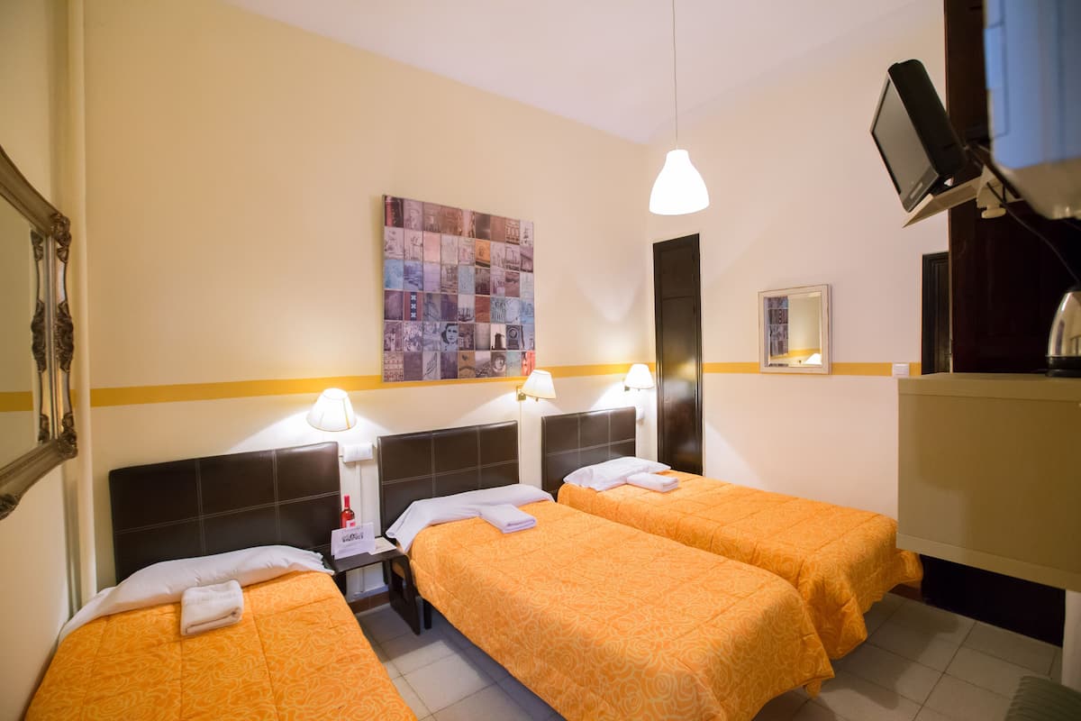 Quarto de hotel com duas camas, uma mesa de cabeceira, uma luminária, um espelho e uma obra de arte na parede.