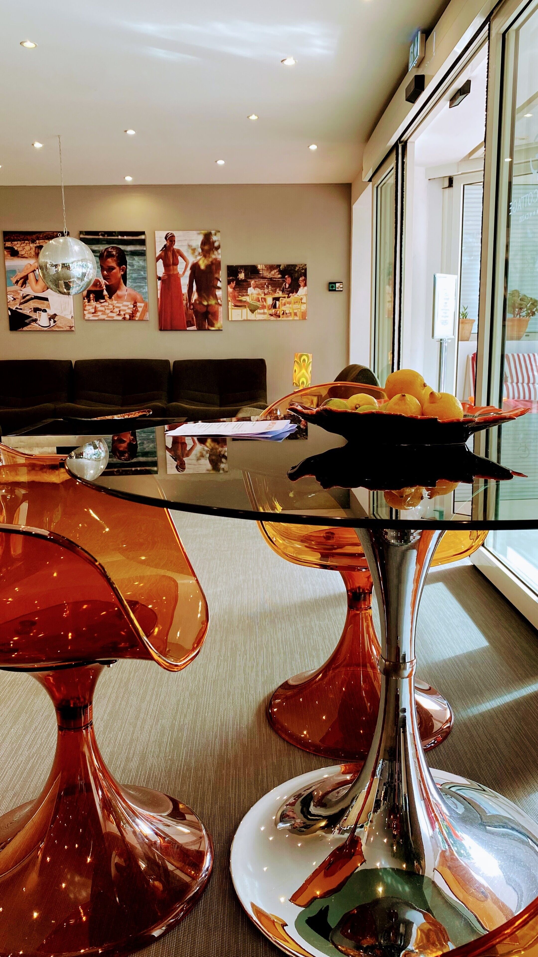 Uma área de refeições moderna com uma mesa de vidro, cadeiras vermelhas e uma exposição de frutas.