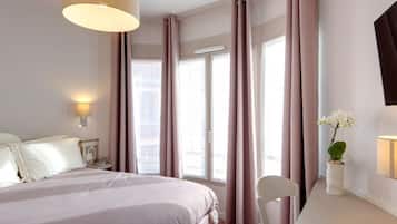 Quarto de hotel com cama, luminárias de cabeceira, televisão e janela com cortinas.