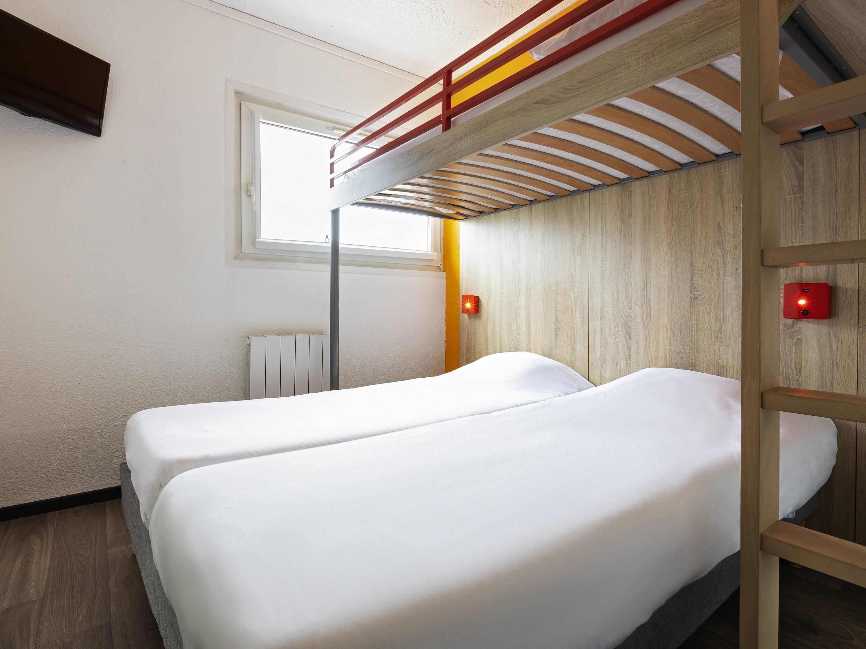 Quarto com duas camas, uma janela, um radiador e uma estrutura de beliche de madeira.