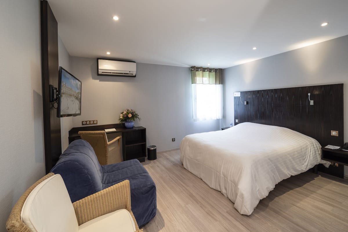 Quarto de hotel moderno com uma cama grande, um sofá, uma escrivaninha com um computador e um ar condicionado.
