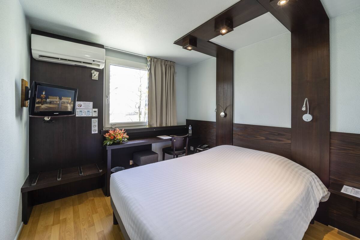 Quarto de hotel com cama grande, escrivaninha com cadeira, televisão e aparelho de ar condicionado.