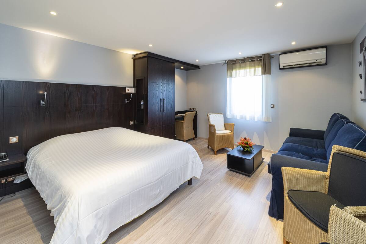 Quarto de hotel com uma cama grande, um sofá, uma cadeira, uma escrivaninha e um aparelho de ar condicionado.