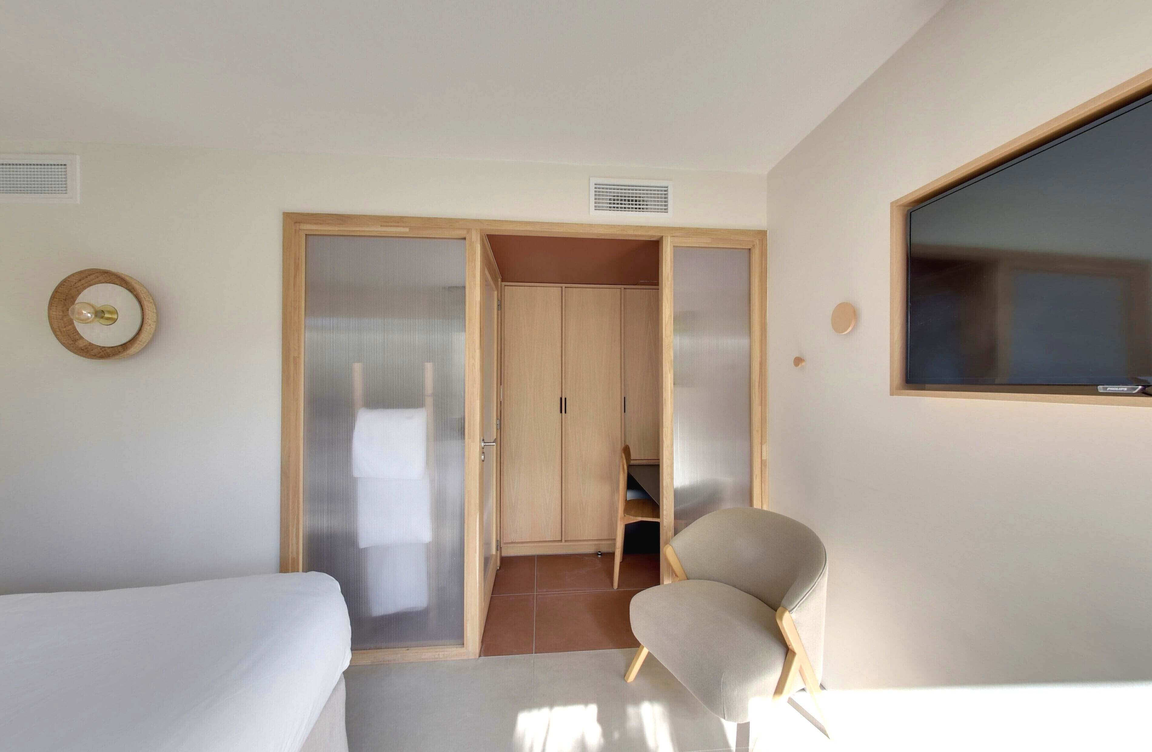 Um quarto com cama, uma cadeira, um guarda-roupa e uma televisão.