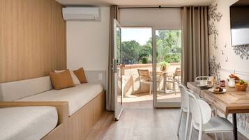 Quarto de hotel moderno com sofá, mesa de jantar, cadeiras e varanda com área de estar.