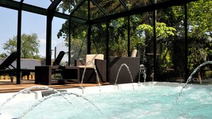 Piscina com jatos de água, rodeada por mobiliário de vime e um revestimento de vidro.