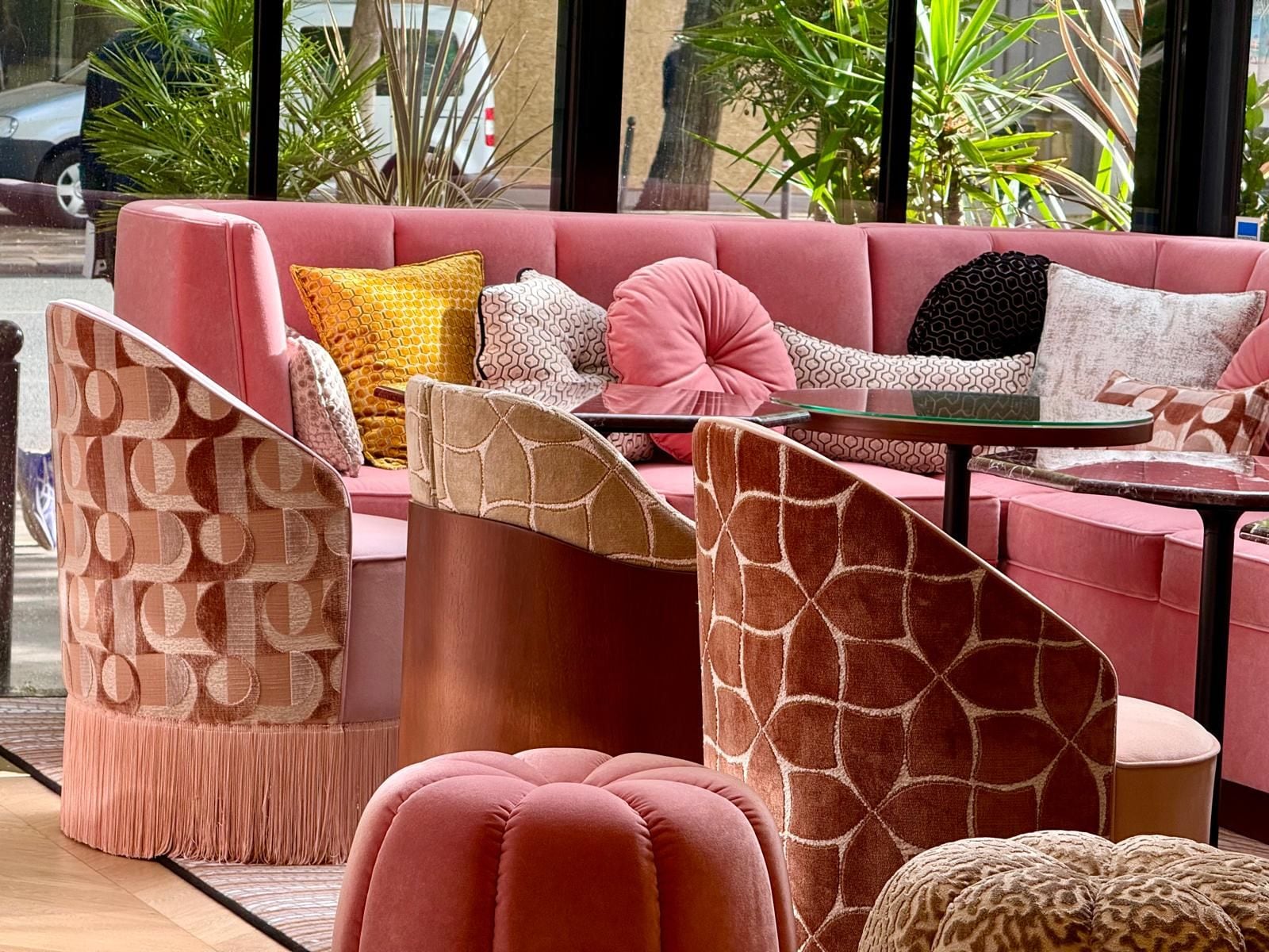 Uma área de estar com um sofá rosa, cadeiras estampadas e uma pequena mesa.