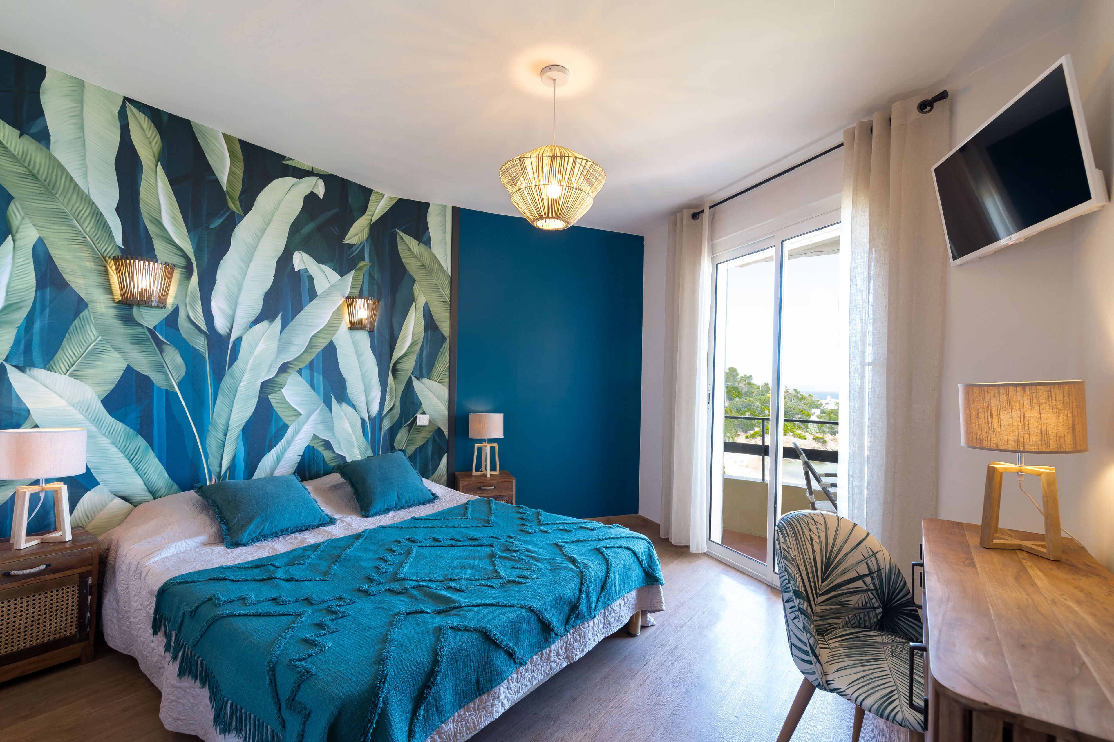 Quarto com cama grande, televisão na parede, escrivaninha com luminária e vista para o exterior.