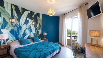 Quarto com cama grande, televisão na parede, escrivaninha com luminária e vista para o exterior.